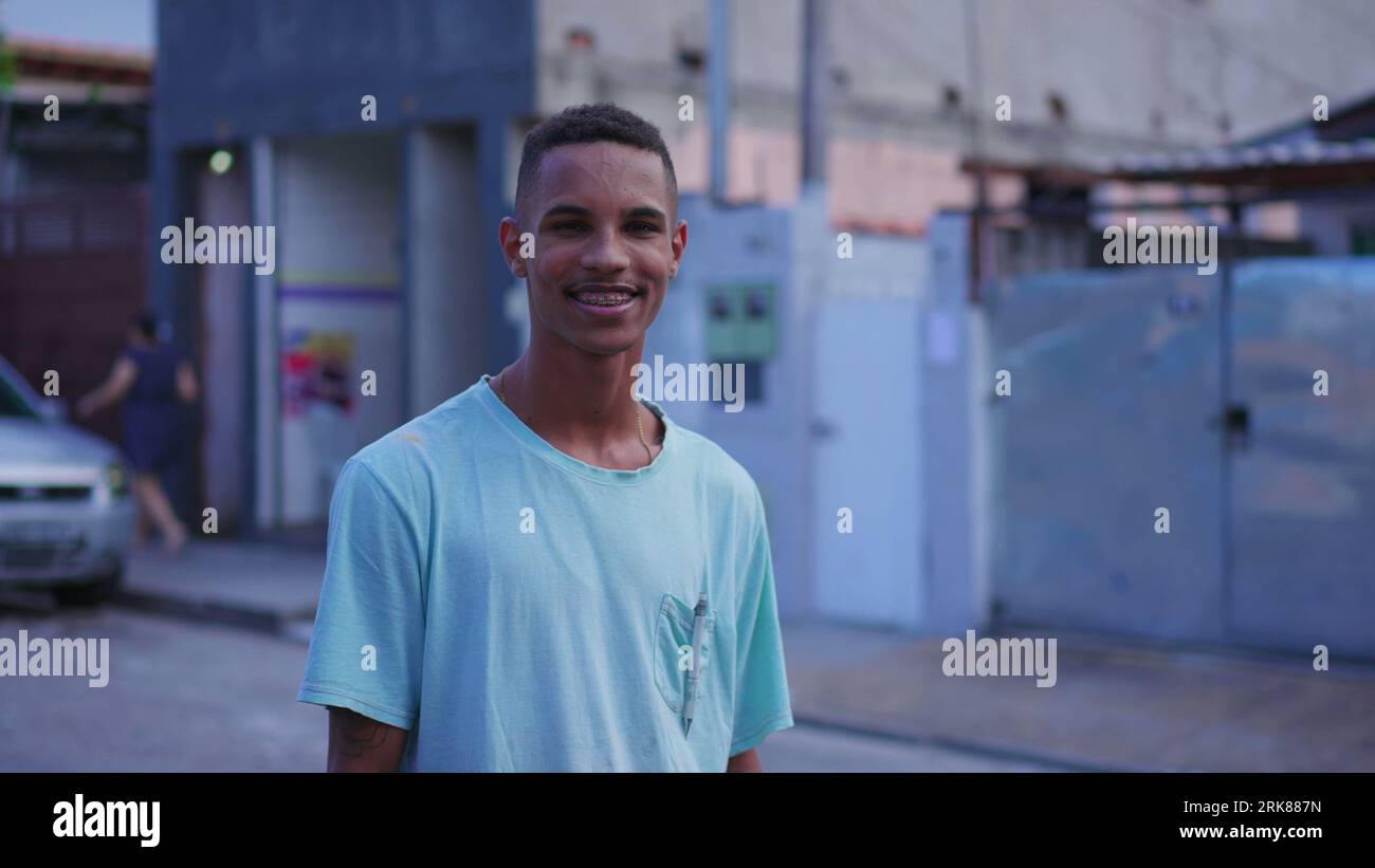 One cheerful black Brazilian young man standing in street smiling at ...