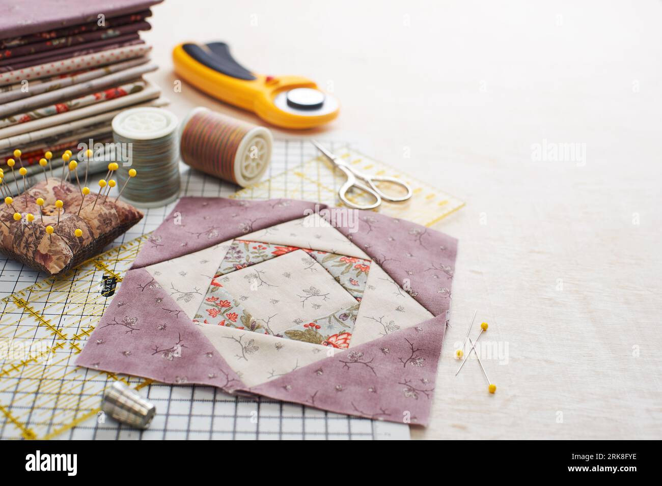 Patchwork block on craft mat, stack of fabric, sewing accessories on ...