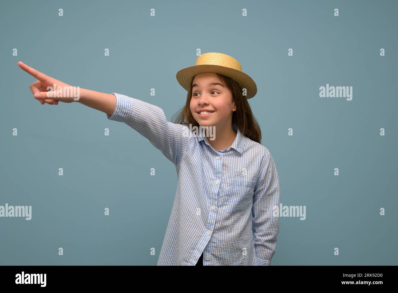 Cute teenage girl in a straw hat and a light blue summer shirt smiles ...