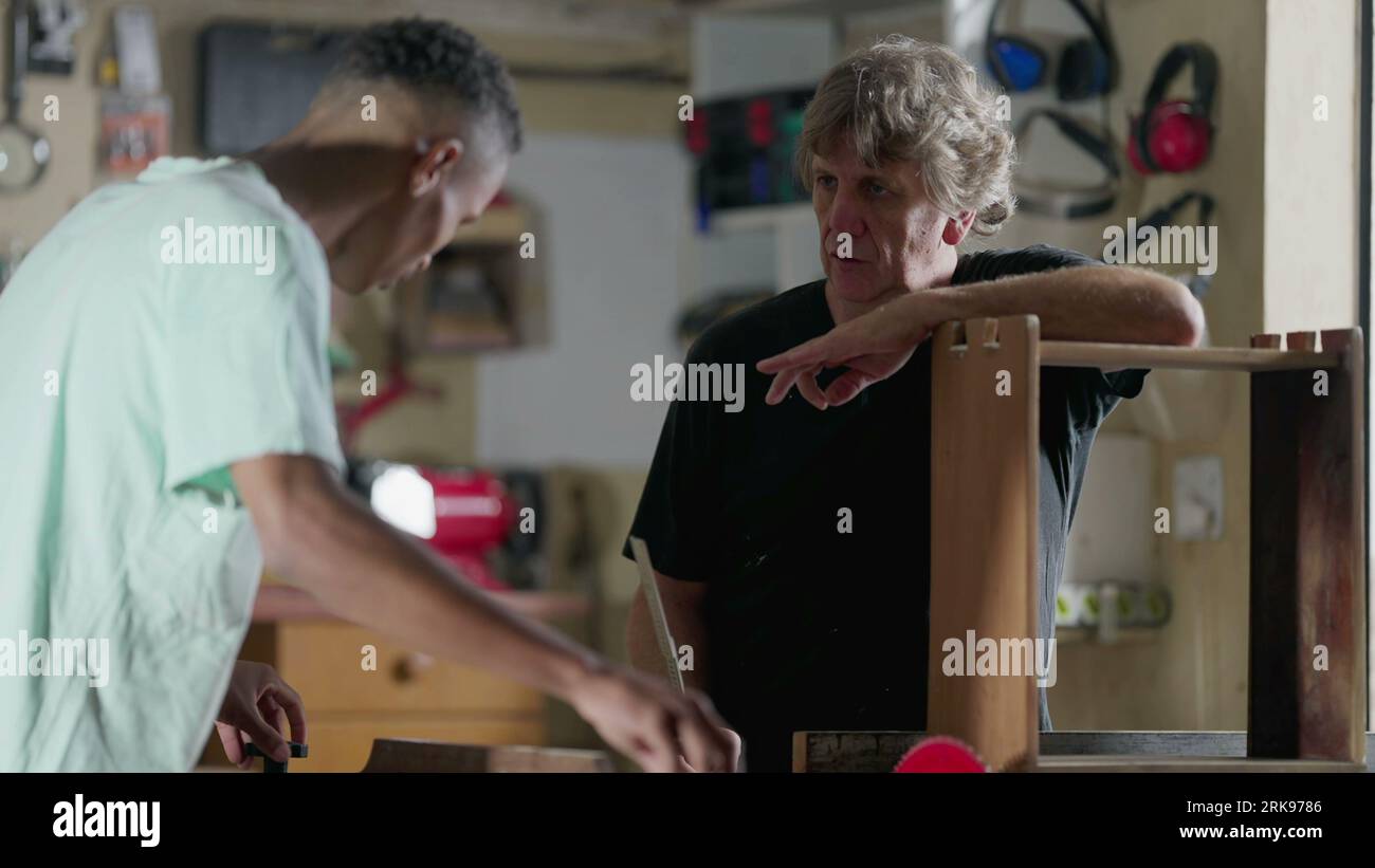 Carpenter orienting apprentice at woodworking carpentry workshop . Candid teacher talking with ...