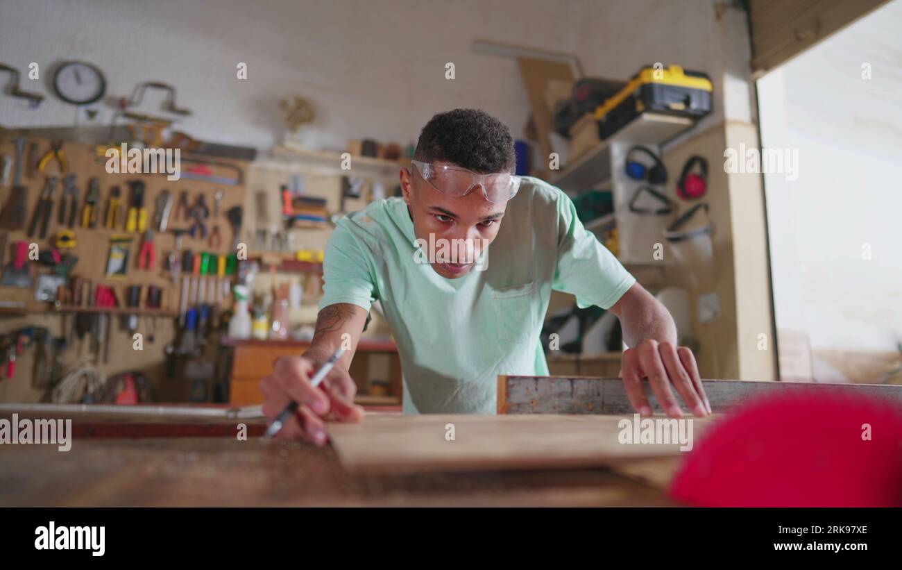One Young black carpentry student measuring wood, preparing to use saw ...