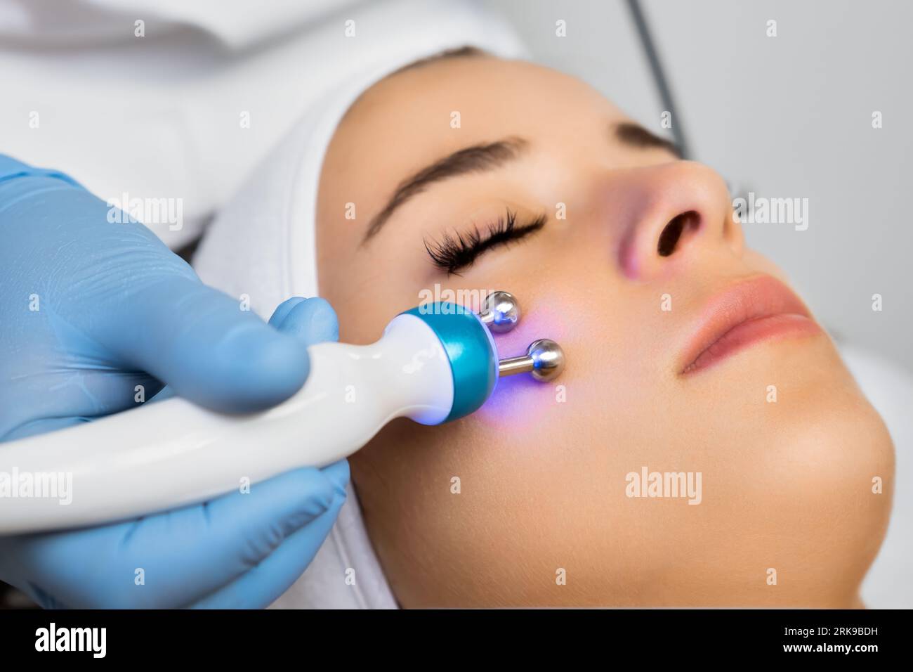 Specialist in rubber gloves uses microcurrent massage device on female ...