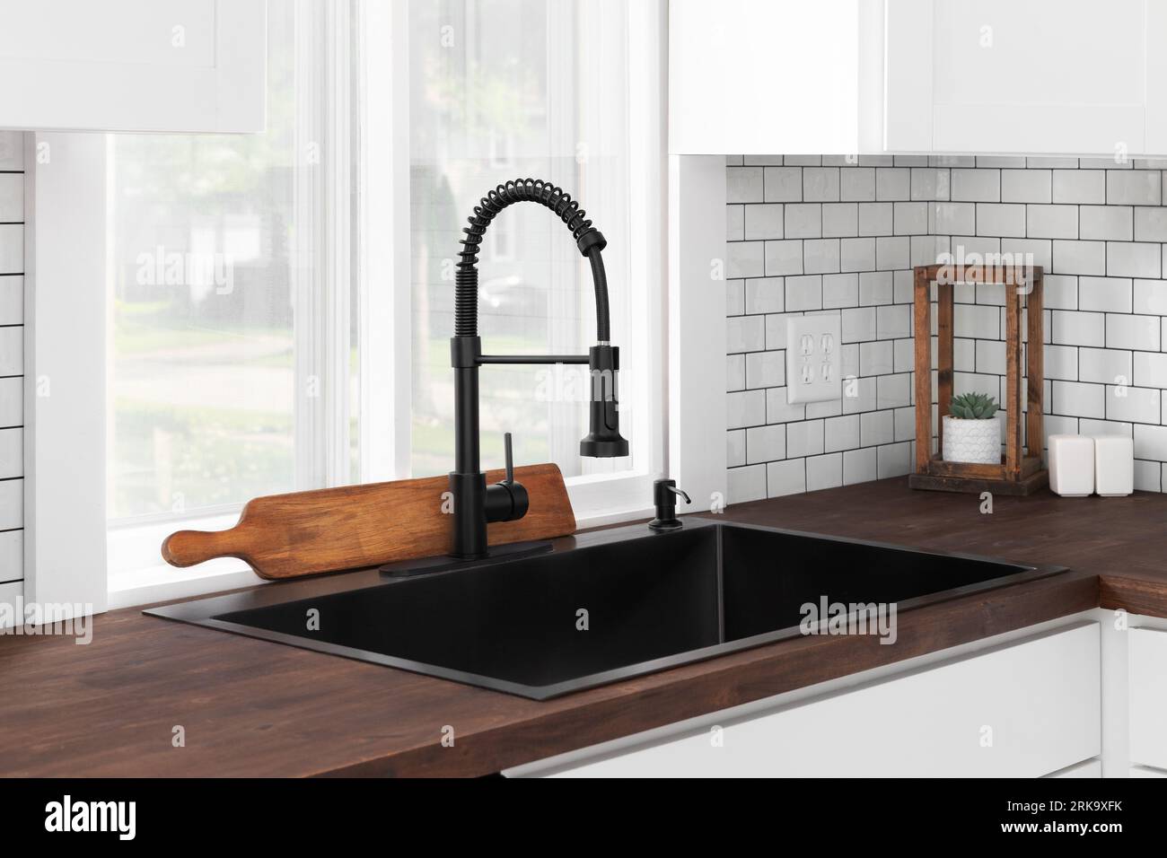 A black kitchen sink and faucet detail in a white kitchen with a ...