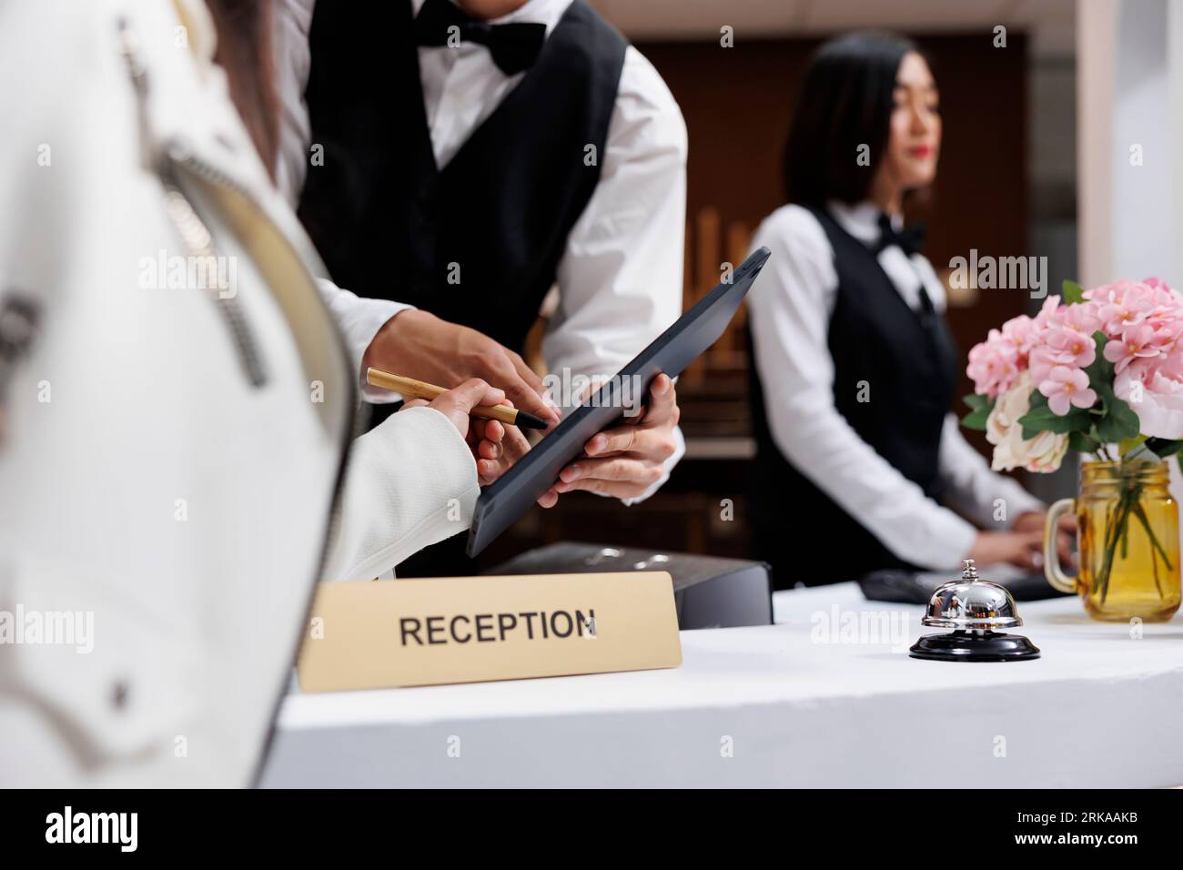 Asian male receptionist at contemporary hotel helps customer sign ...