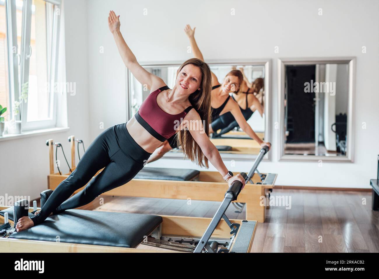 Two smiling fit-shaped females doing side plank with raised arm static ...