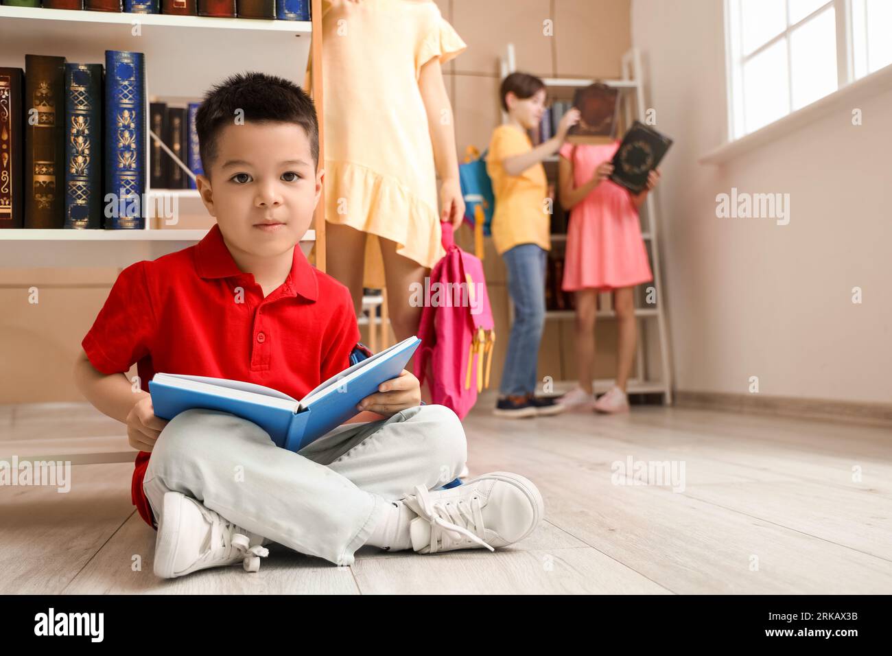 Cute little boy reading book in library Stock Photo - Alamy