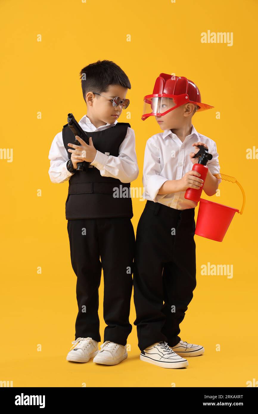 Cute little policeman and firefighter on yellow background Stock Photo ...