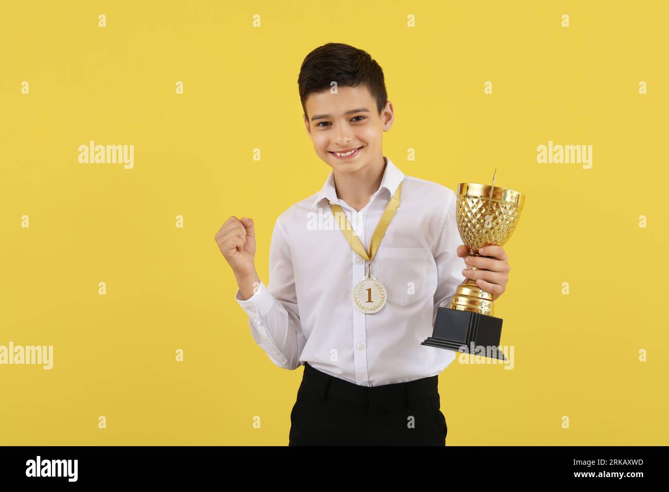 Smart little school boy with prize cup and medal on yellow background ...