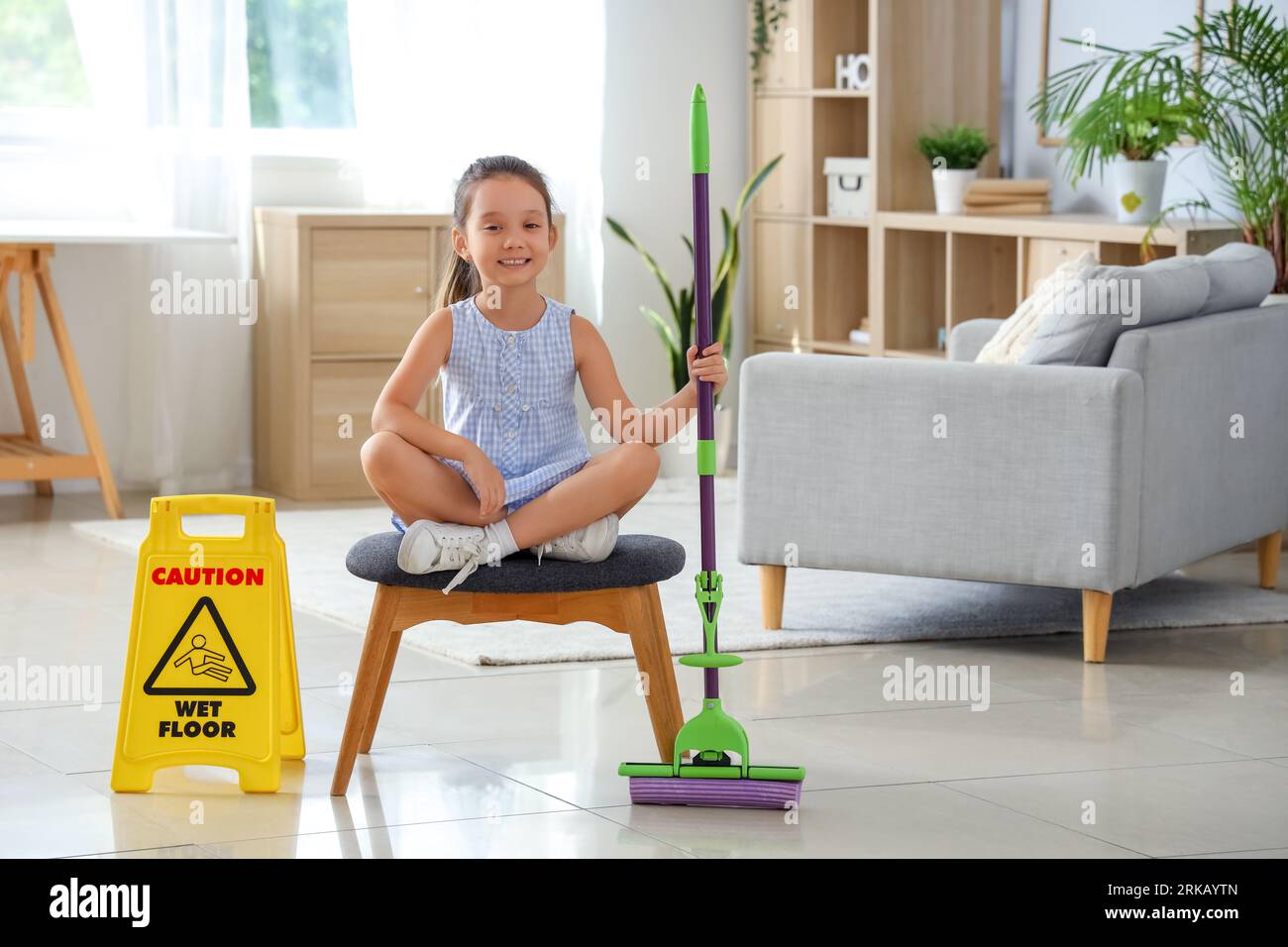 Cute little girl with mop and caution sign at home Stock Photo - Alamy