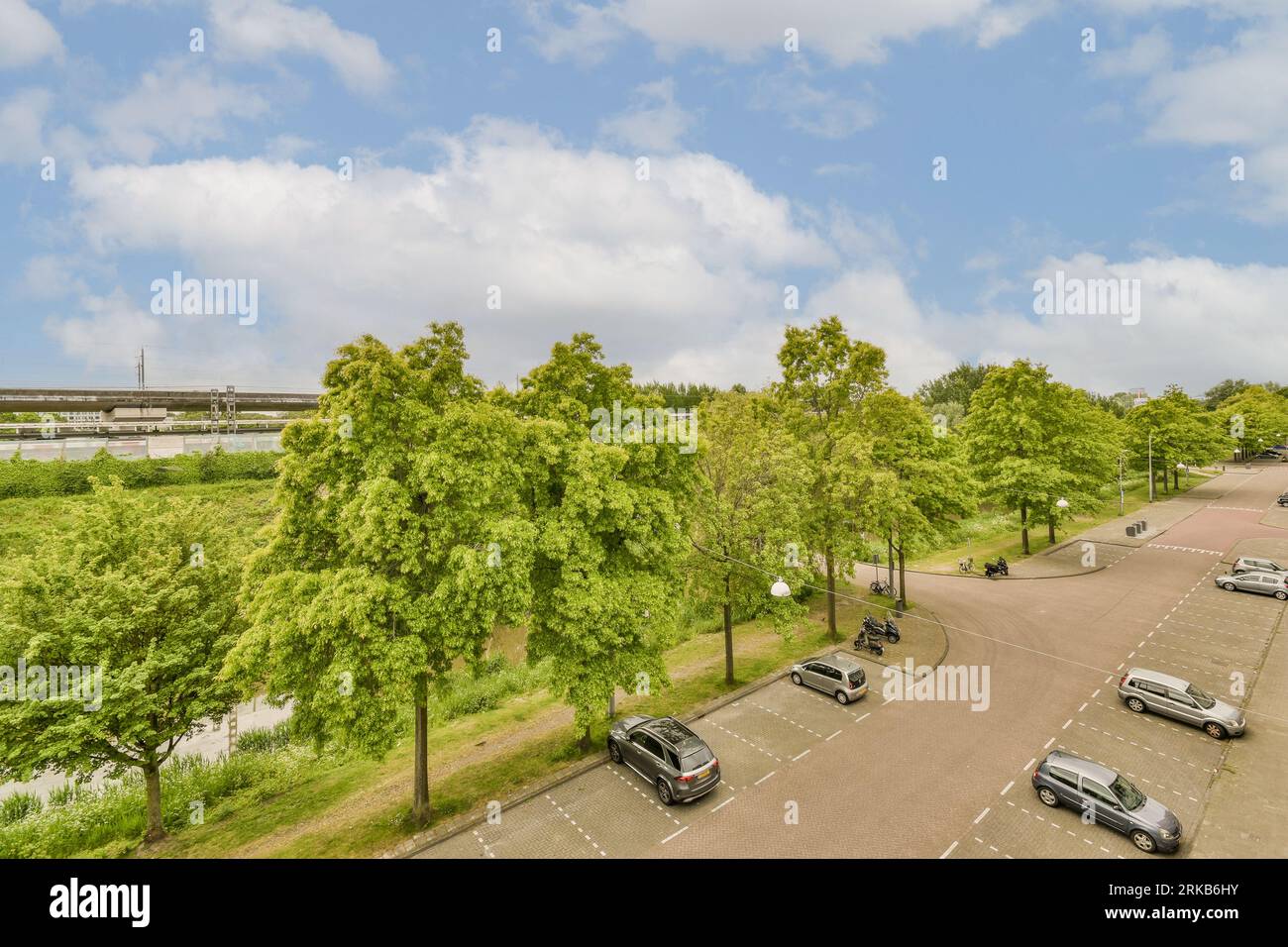 a street with cars parked on the side and green trees in the middle ...