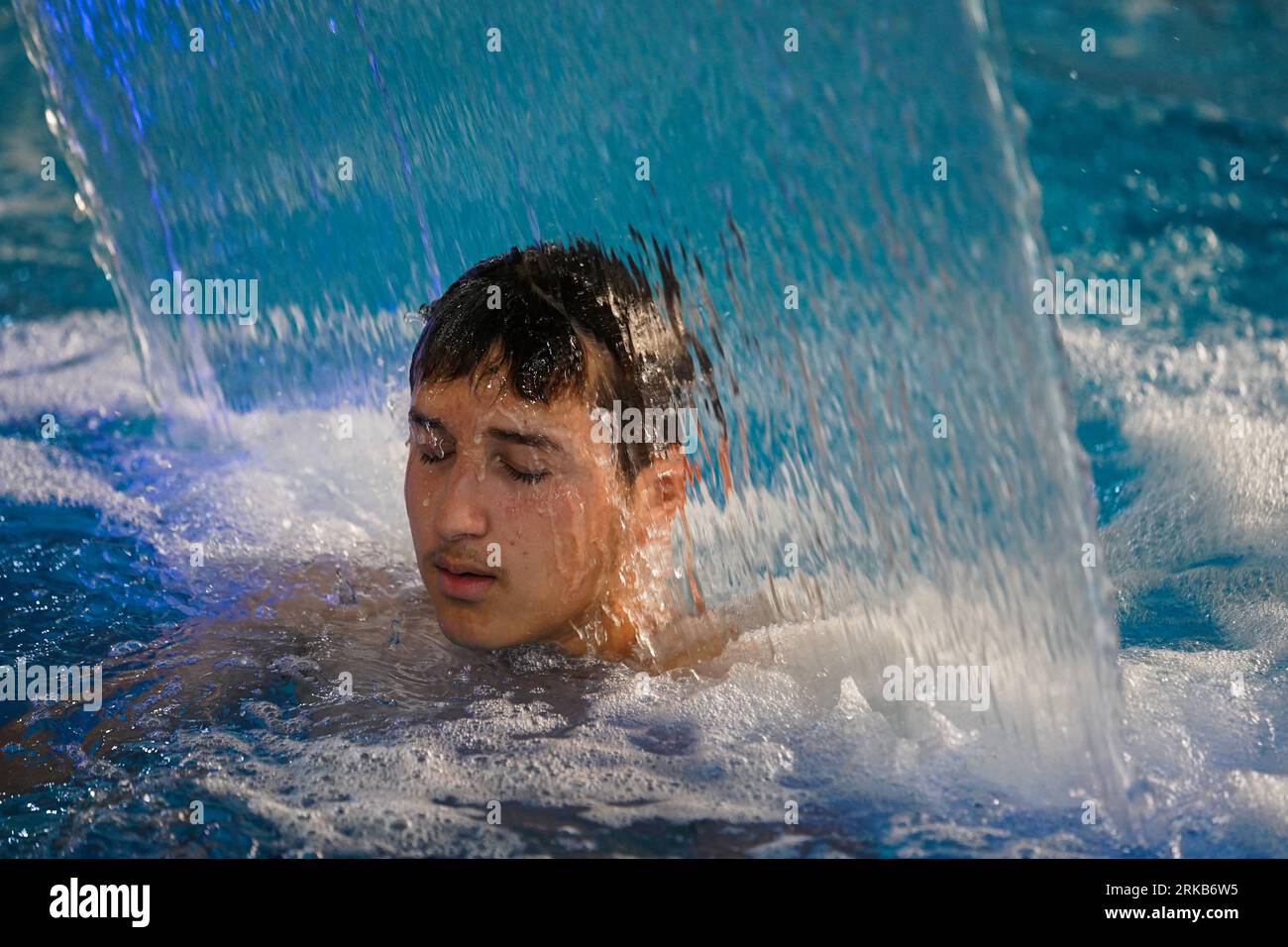 A young man cools himself in a swimming pool on a hot summer day. In ...