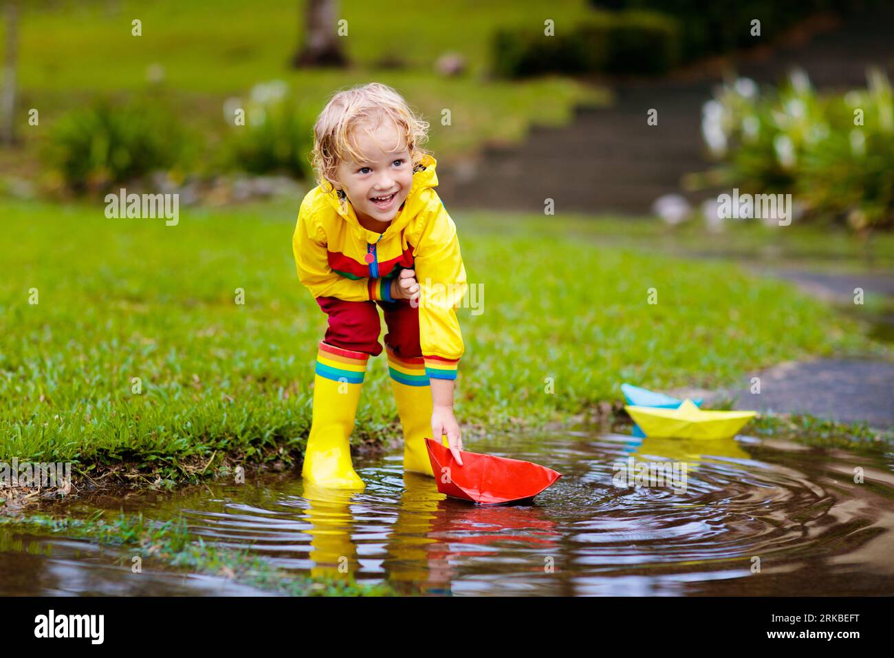 Child playing with paper boat in puddle. Kids play outdoor by autumn ...