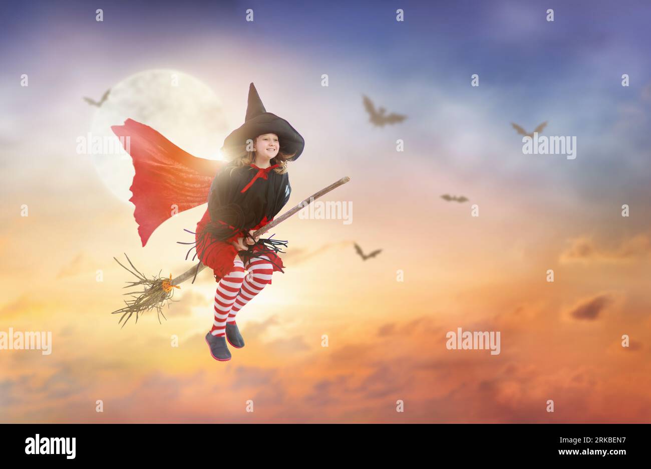 Little witch flying broom on Halloween night. Huge full moon and bats ...