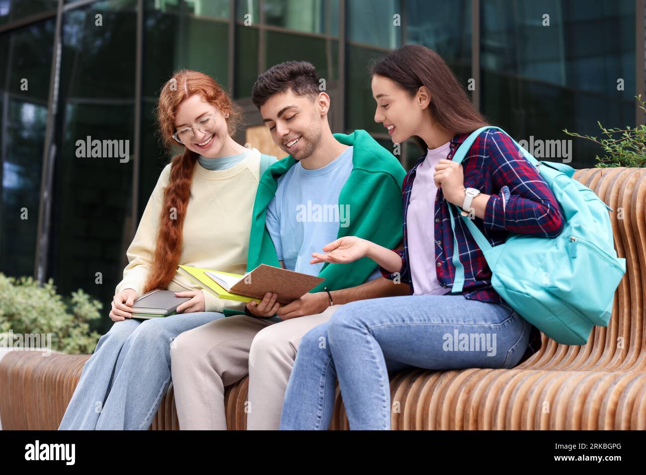 Happy young students studying with notebooks on bench outdoors Stock ...