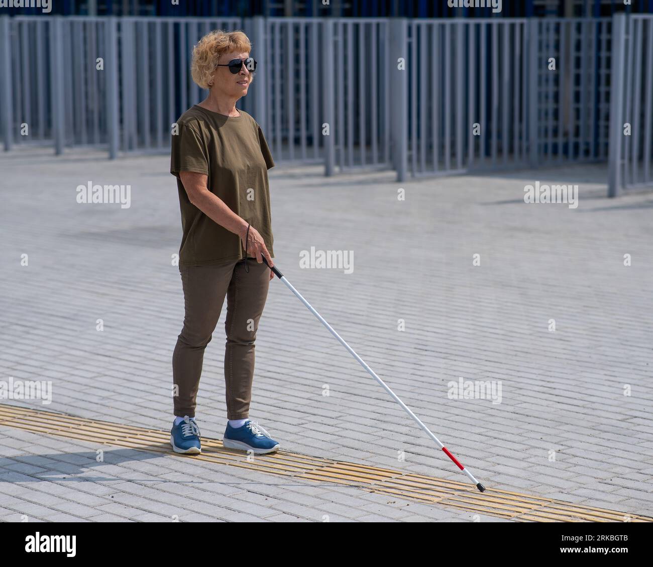 An elderly blind woman walks with a cane along a tactile tile Stock ...