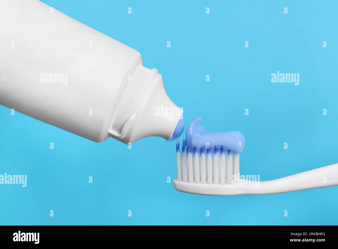 Applying paste on toothbrush against light blue background, closeup ...