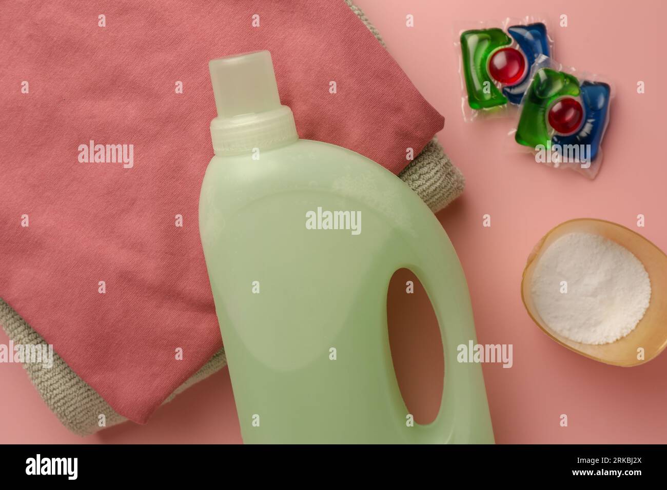 Bottle of fabric softener, stacked clean clothes, laundry capsules and ...