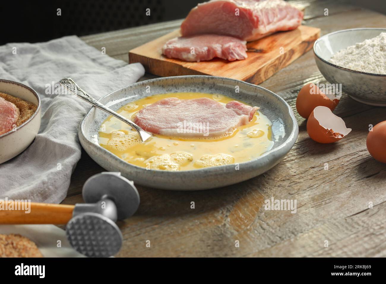 Cooking schnitzel. Raw pork chop in eggs, meat mallet and ingredients ...