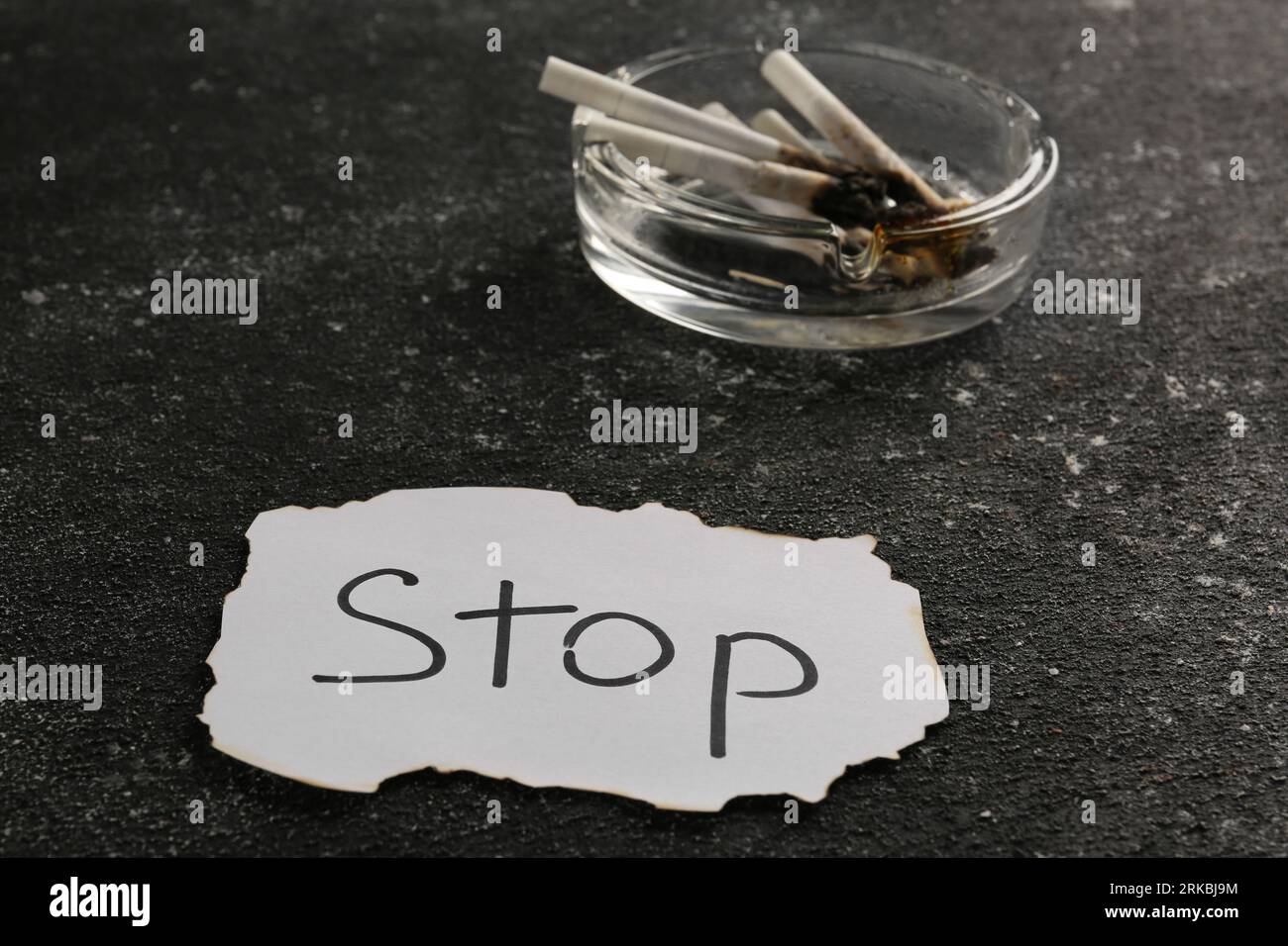 Ashtray with burnt cigarettes and word Stop written on paper on black ...