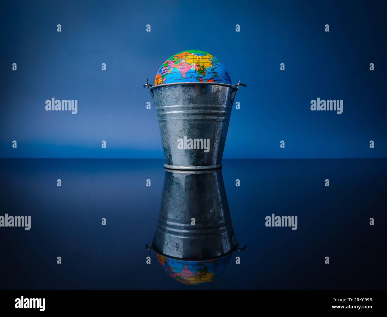 Earth globe in a steel bucket with reflection on a black acrylic board ...