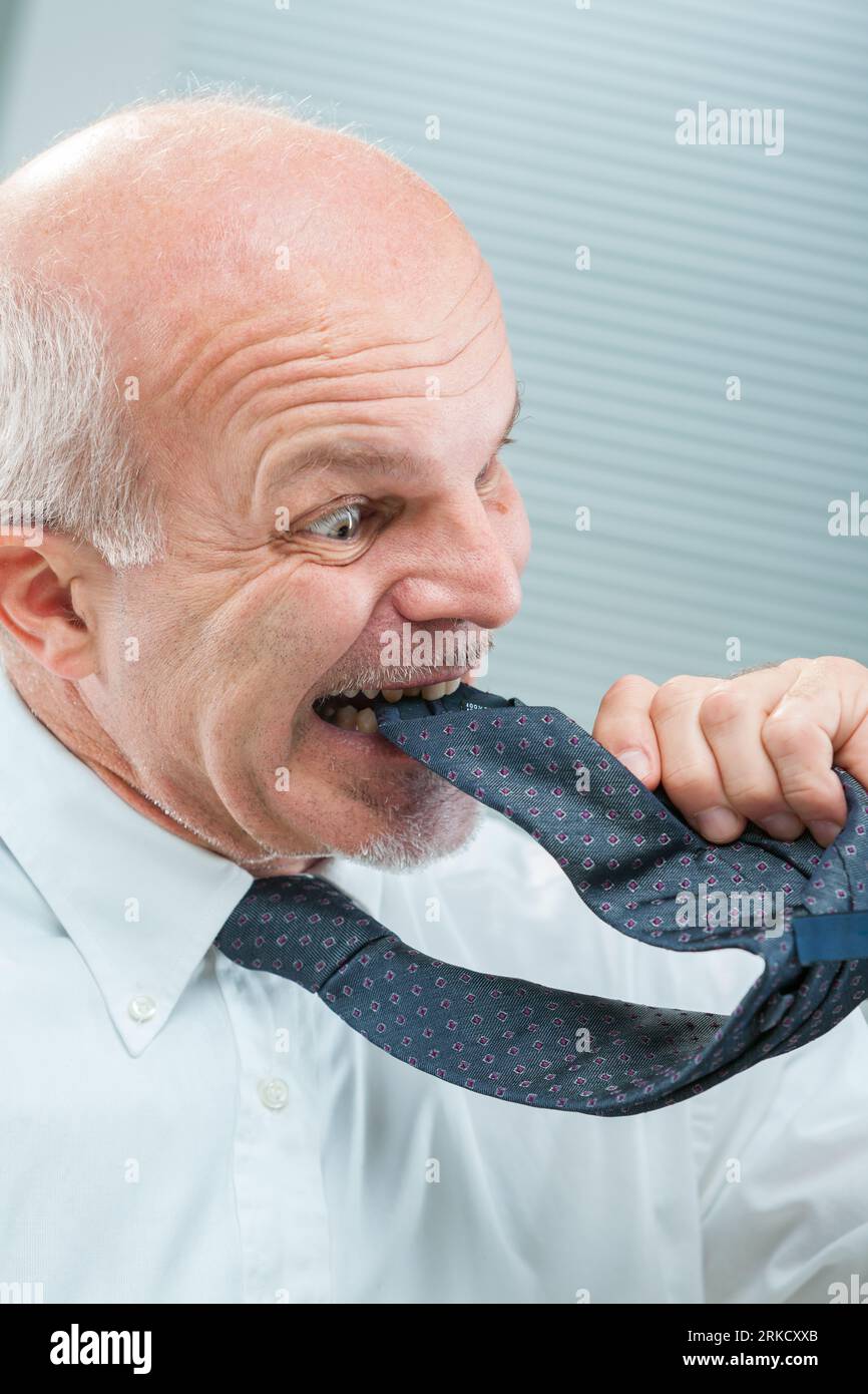 distressed senior businessman bites his tie in an impulsive act. Driven ...