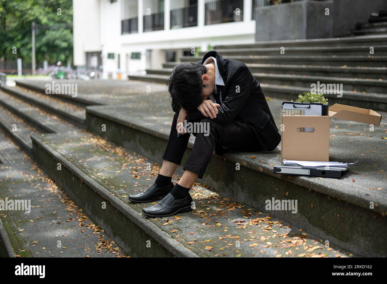 A depressed and stressed young Asian businessman sits on the stairs in ...