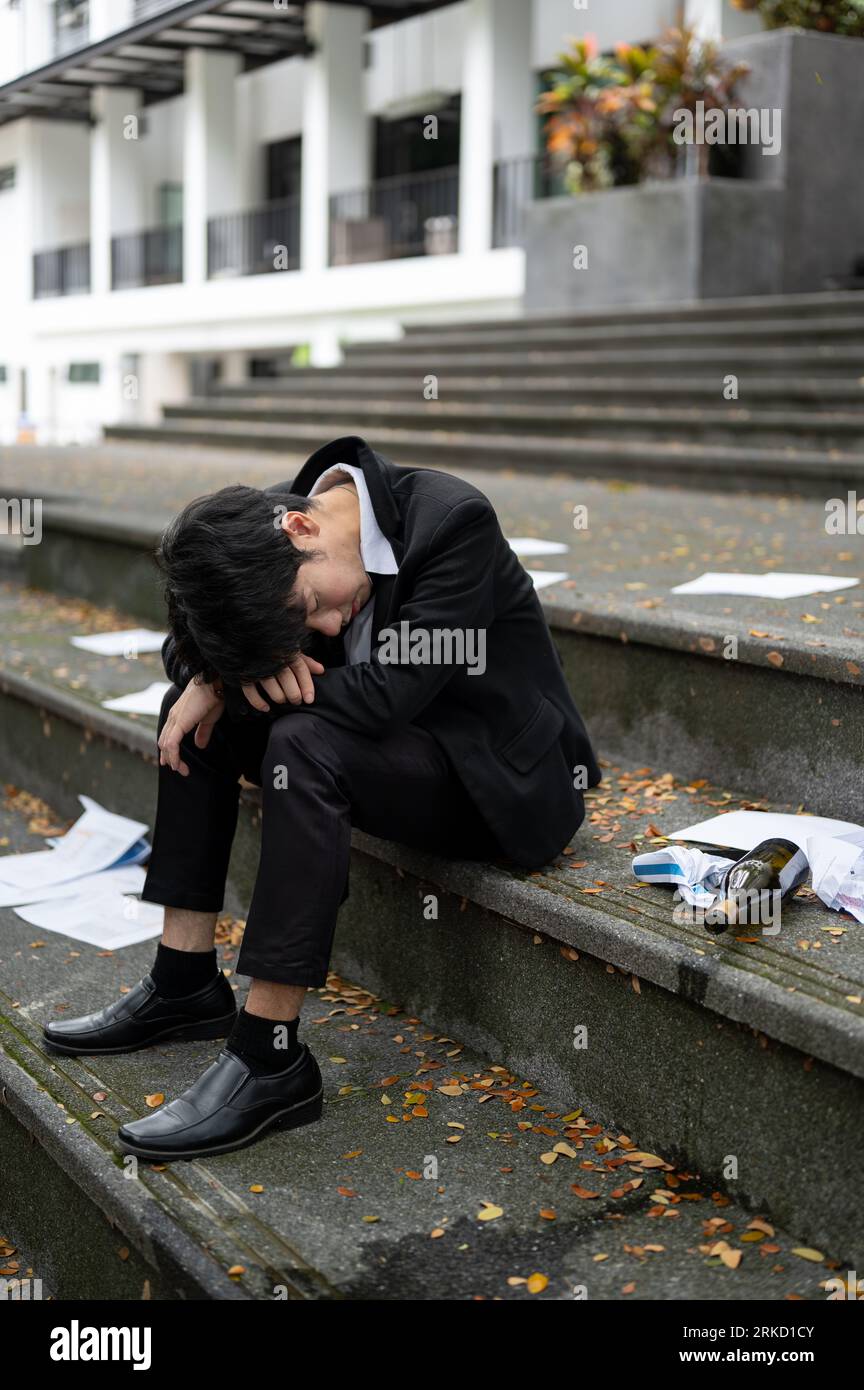 A drunk, depressed, and hopeless Asian businessman sits on the stairs ...