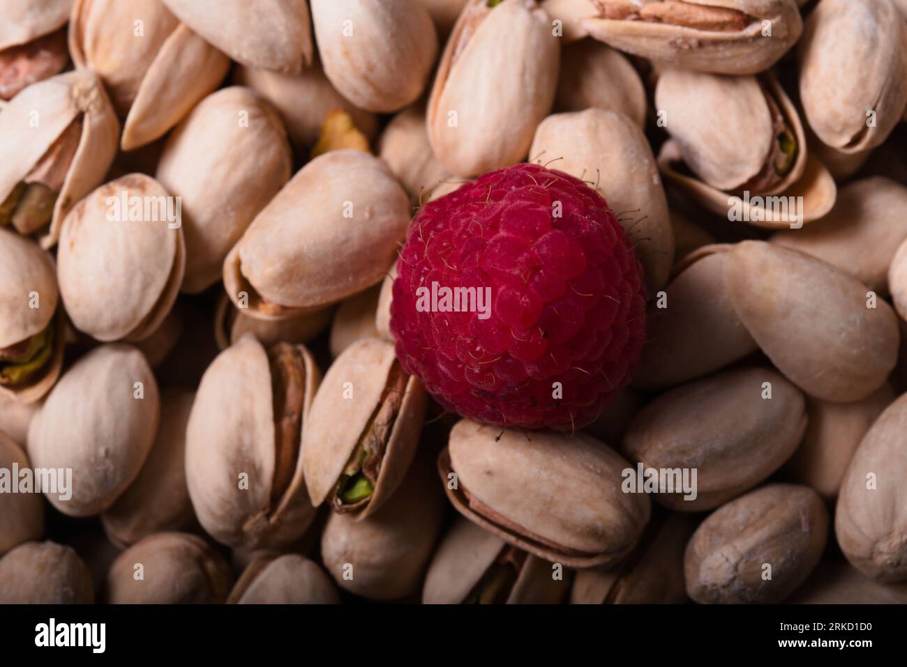 Closeup of tasty pistachio nuts with a single raspberry delineating ...