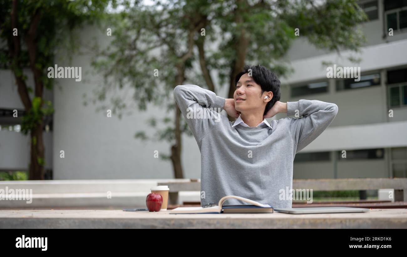 A happy and relaxed young Asian male university student is stretching ...