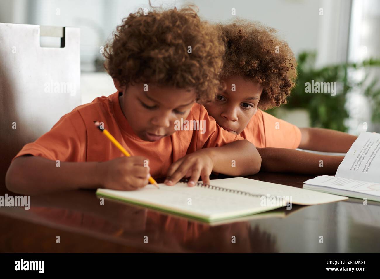 Curious boy looking how his brother writing in notebook when doing ...