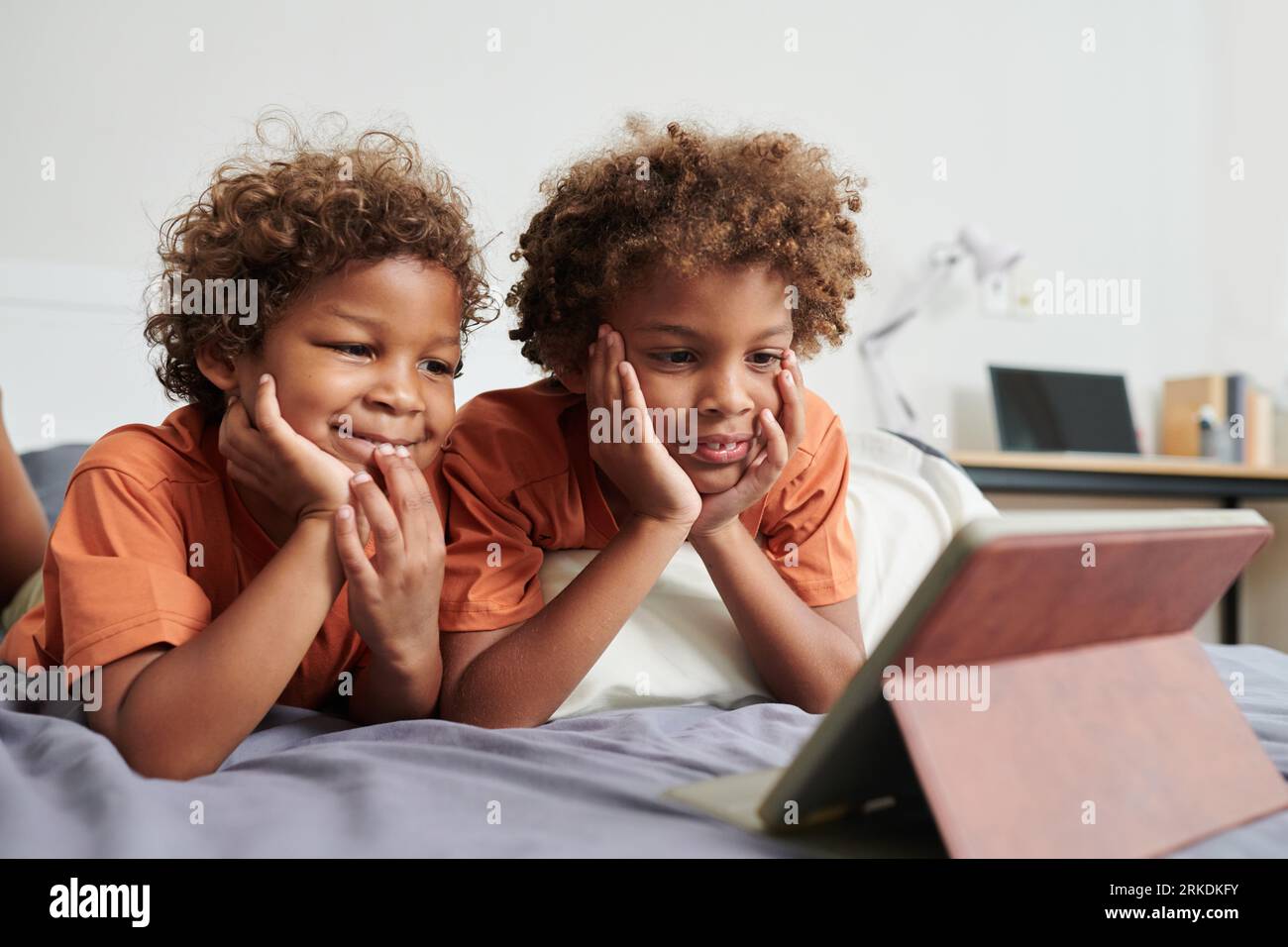 Smiling kids watching cartoon on tablet computer when relaxing on bed ...