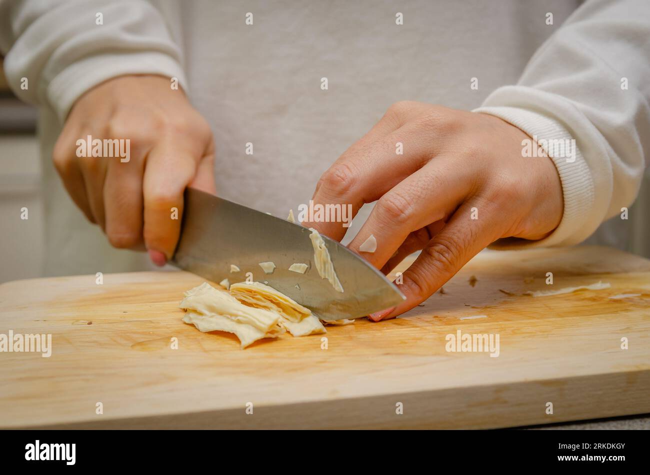 Female cutting tofu skin, yuba with knife on the wooden chopping board ...