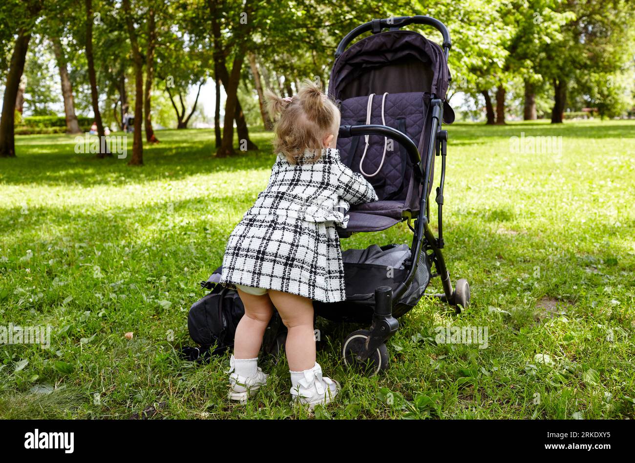 Baby pushing a stroller on a walk in summer park. Adorable little girl ...