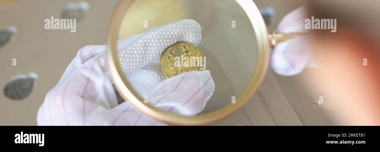 Numismatist in gloves looks through magnifying glass and evaluates ...