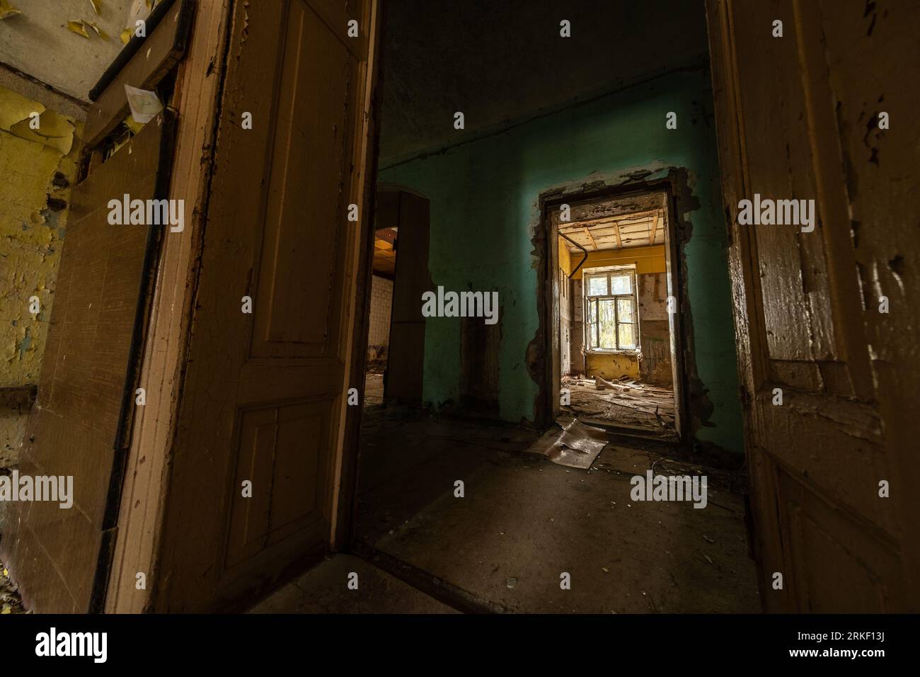 Corridor with white and green shabby walls and big doorways inside old abandoned destroyed ...
