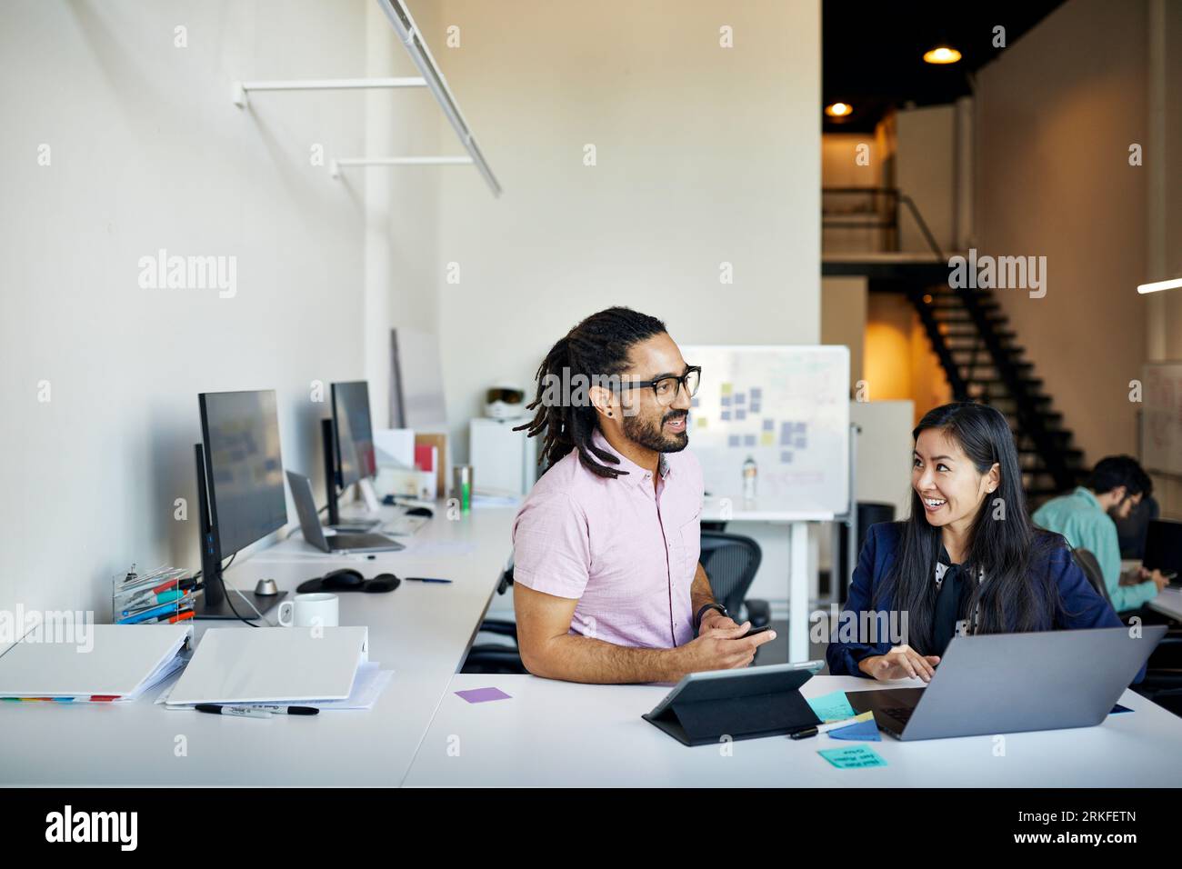 Smiling colleagues talking while doing research over laptop computer on ...
