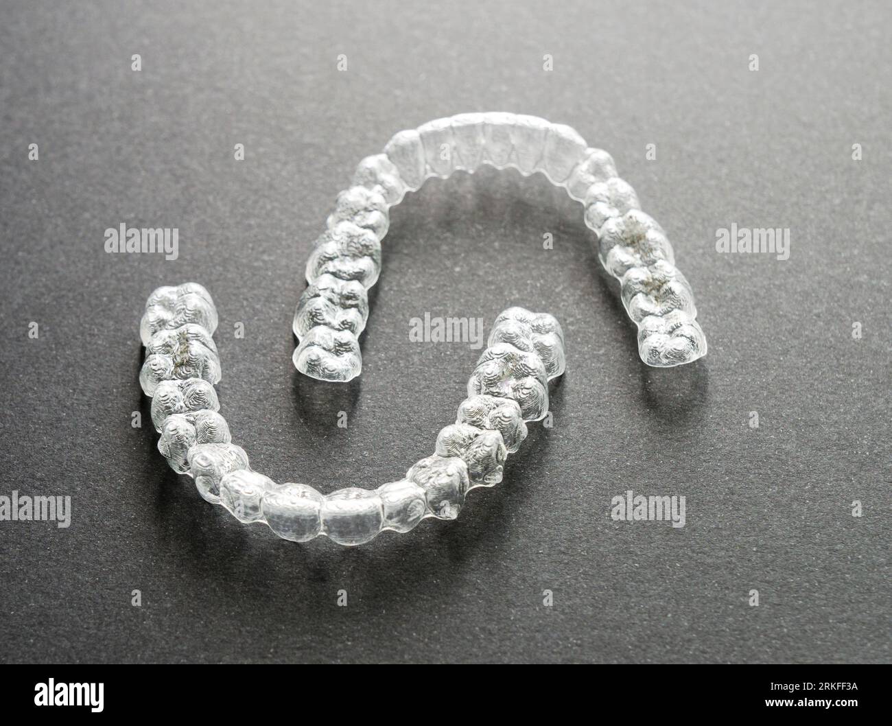 A close-up of clear orthodontic aligners splints on a gray surface ...