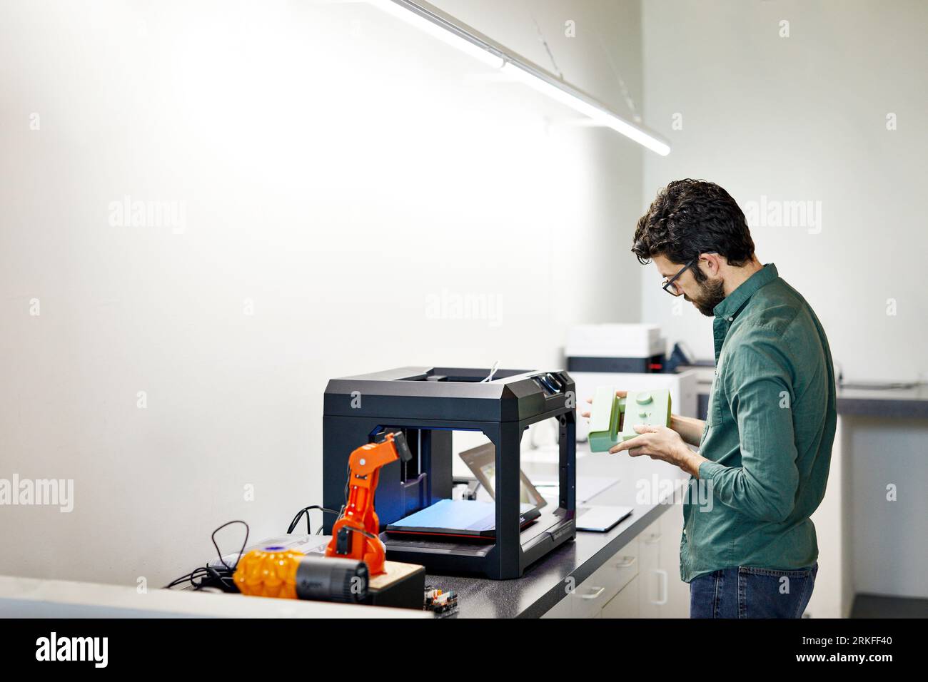 Side view of businessman examining model while standing by 3D printer ...