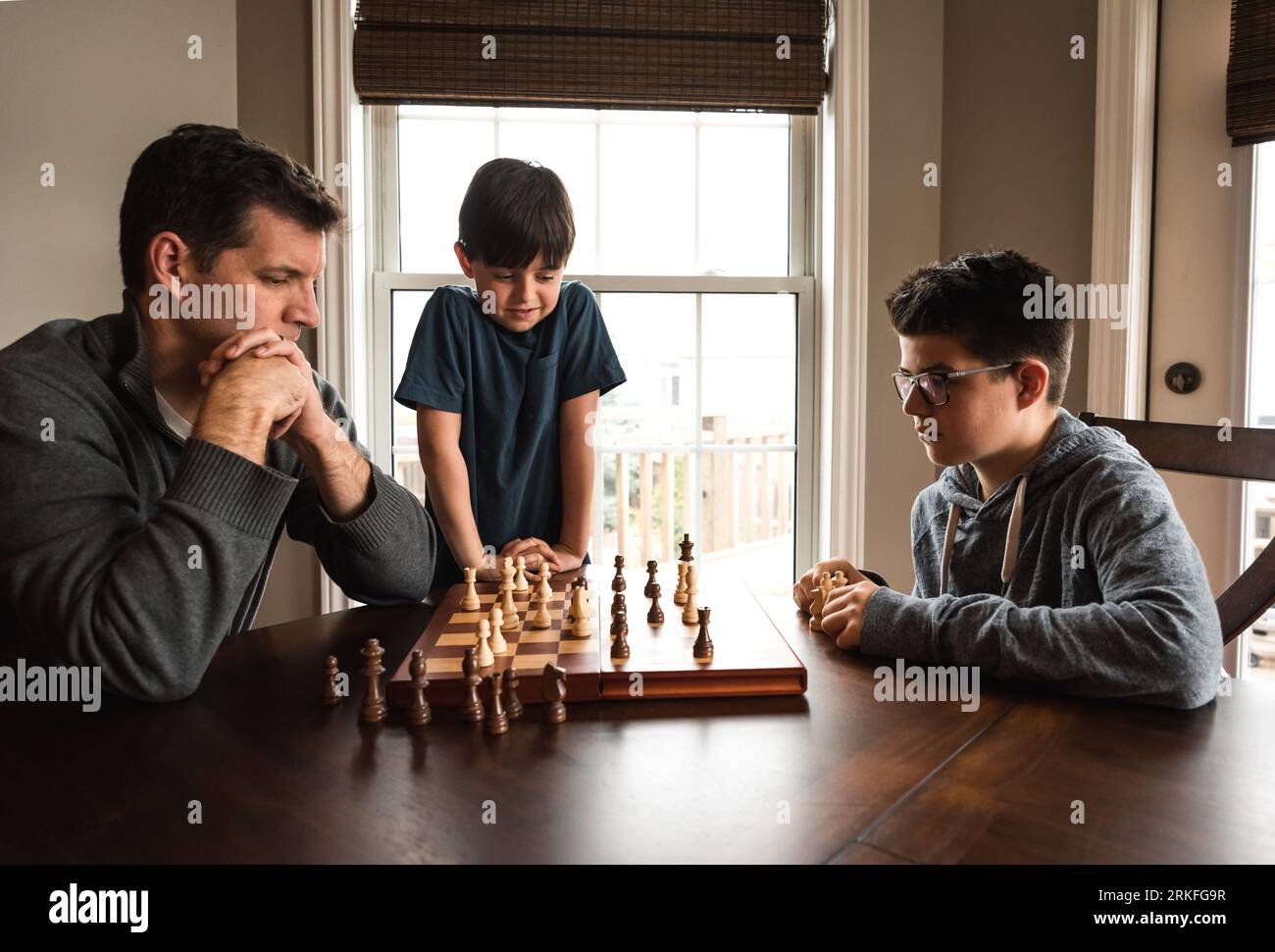 Father and son playing chess at a table while little brother watches ...