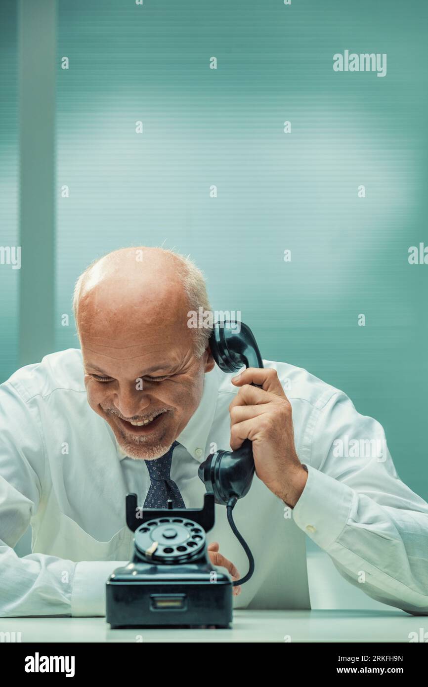 Overwhelmed by laughter, a mature businessman crouches with a phone ...