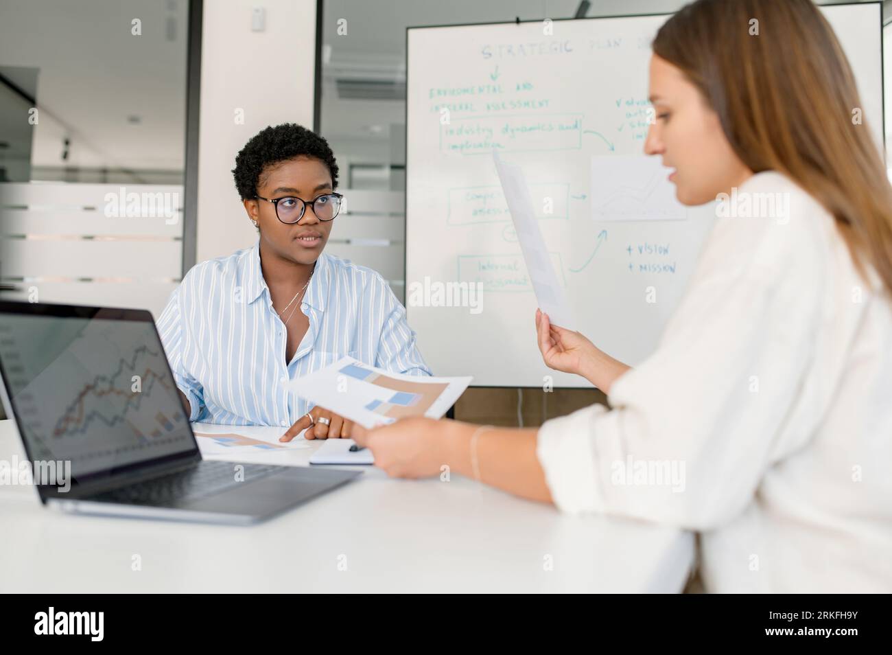 Two businesswomen sitting at the desk and discussing. Diverse female ...