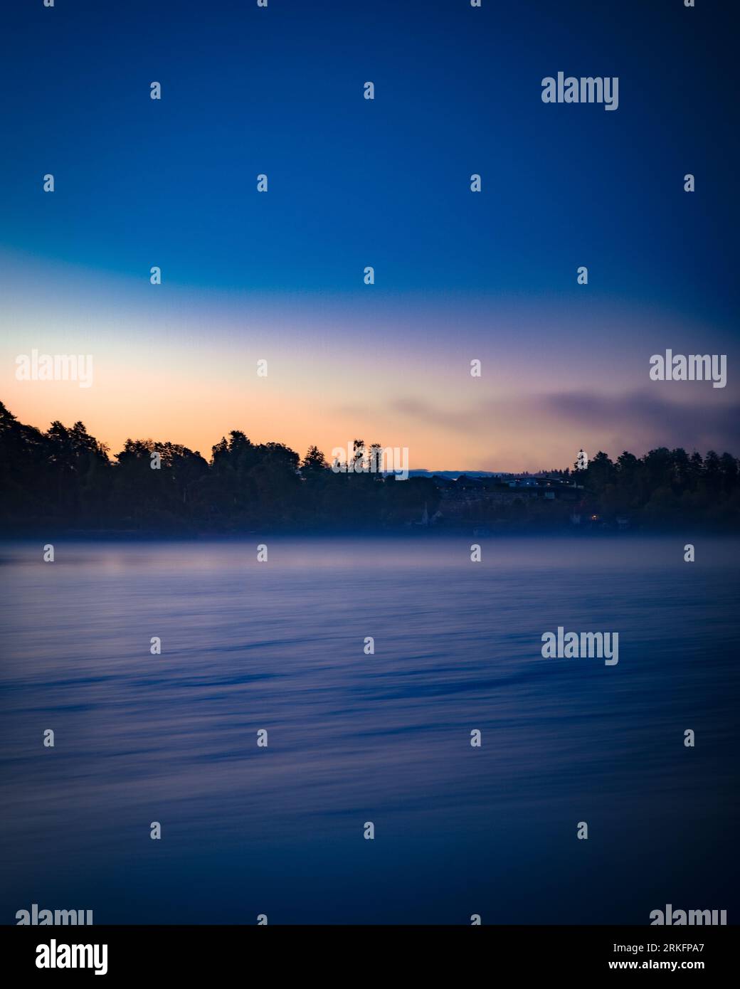 A serene lake enveloped in soft misty fog, illuminated by the fading ...