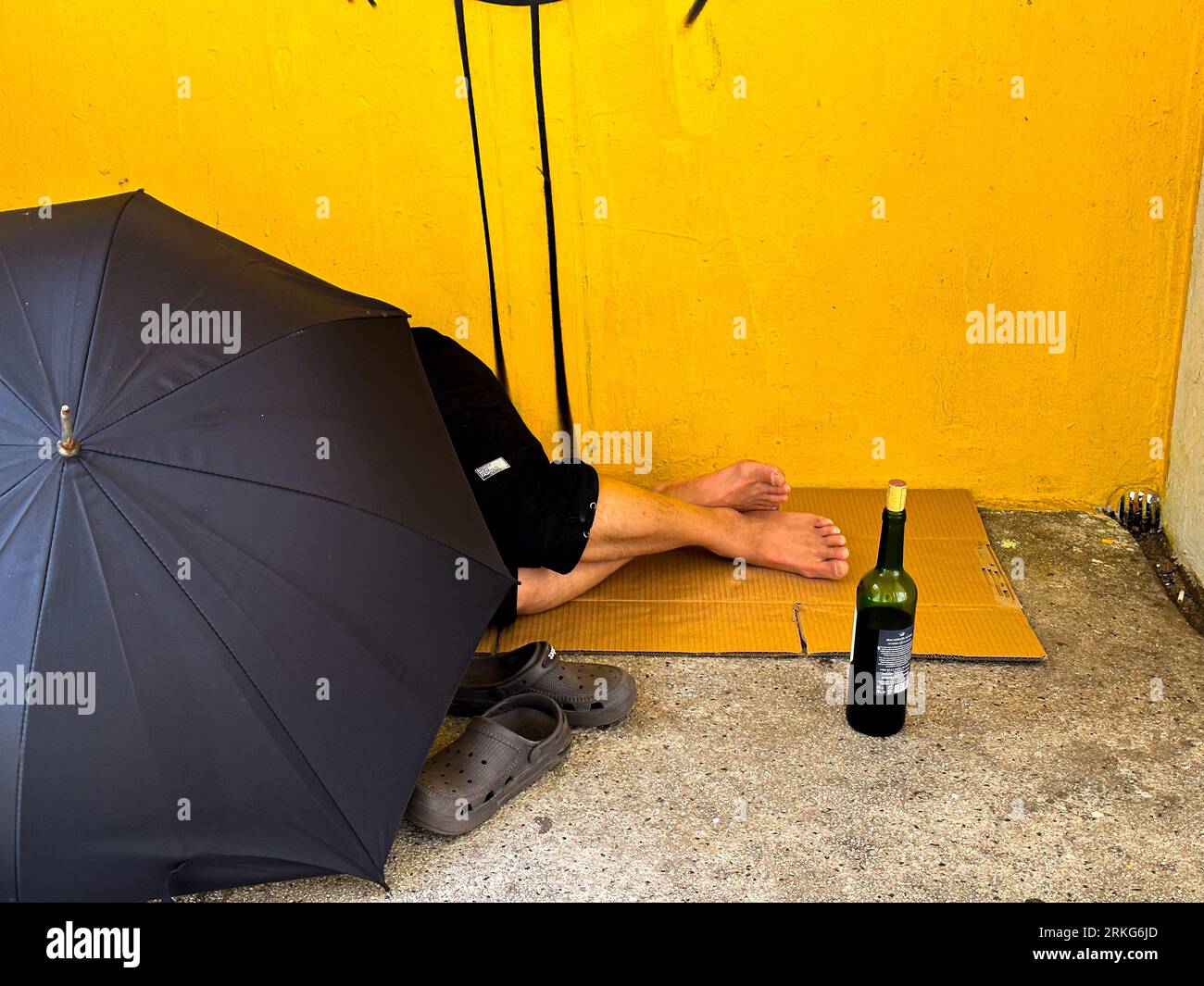 Poor and drunk man sleeping on behind the umbrella at sidewalk with ...