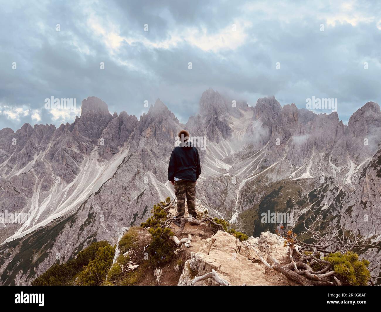 A man standing atop a mountain peak and surveying the rocky terrain ...