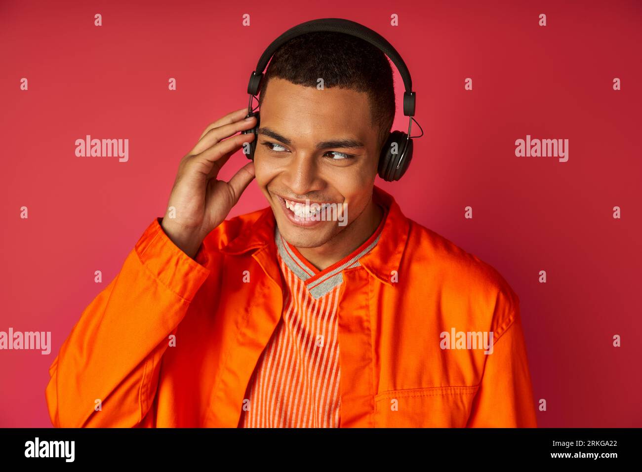 smiling african american man in orange shirt and wireless headphones ...