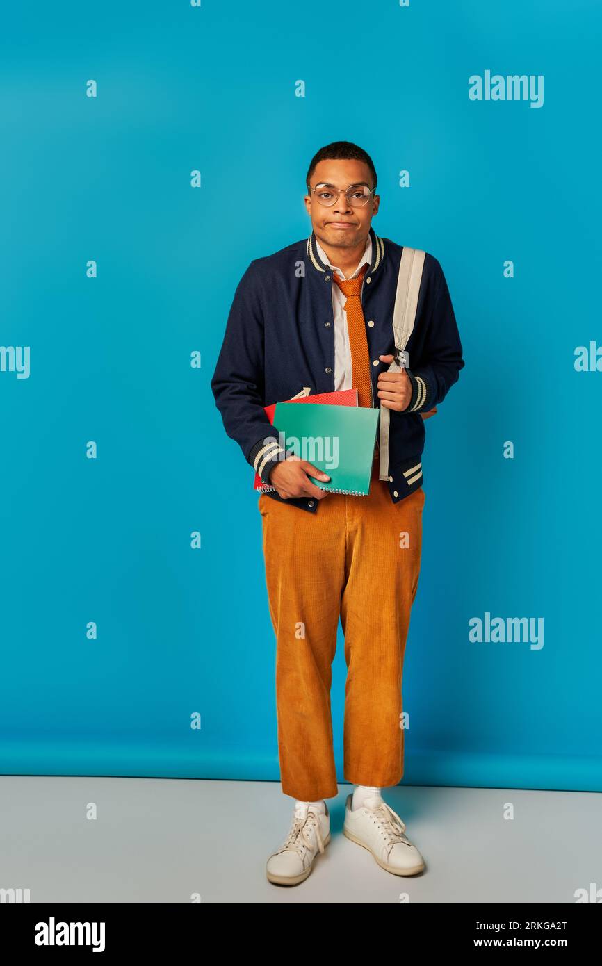 bored african american student with notebooks and backpack puffing ...
