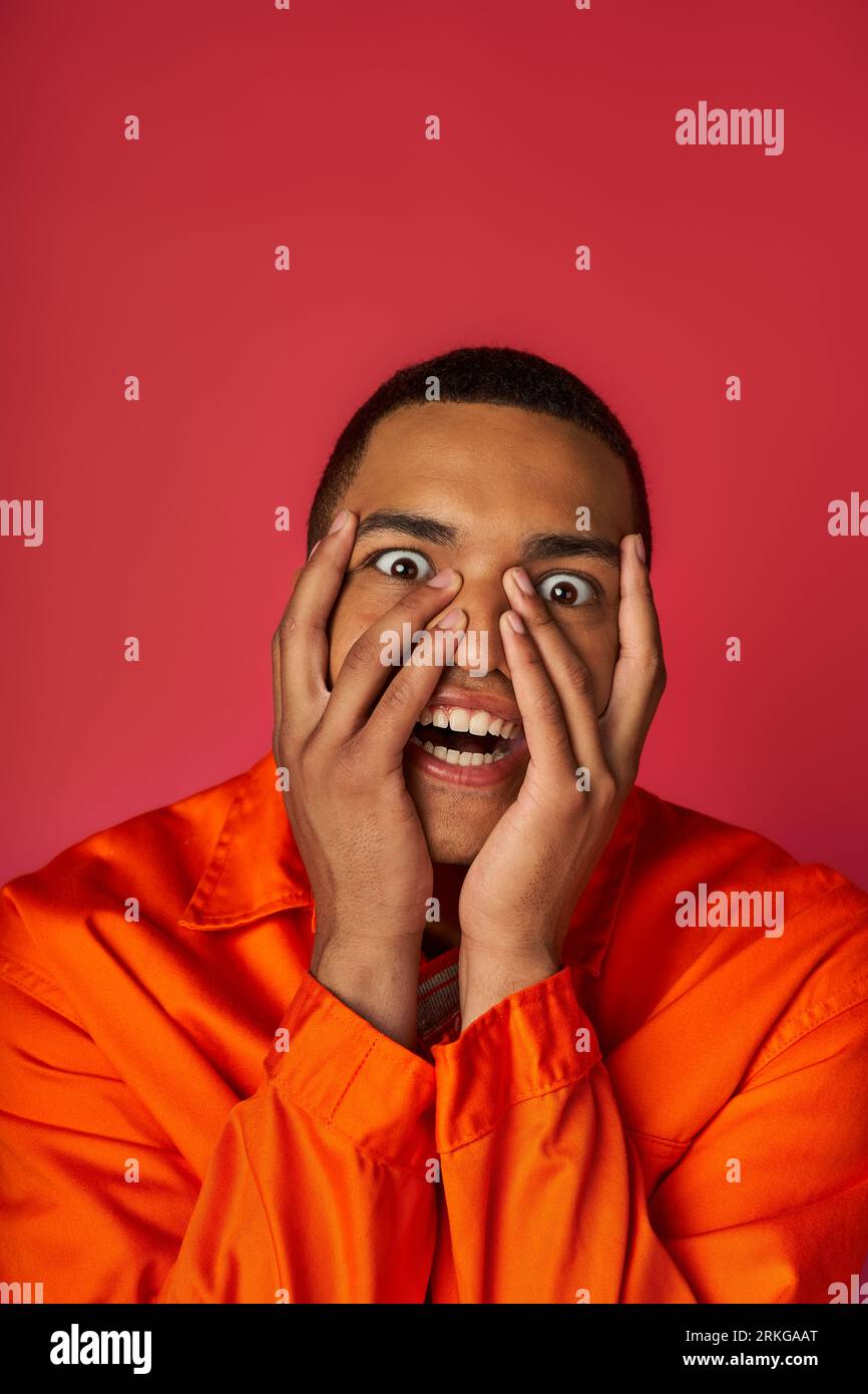 scared african american man in orange shirt obscuring face with hands ...