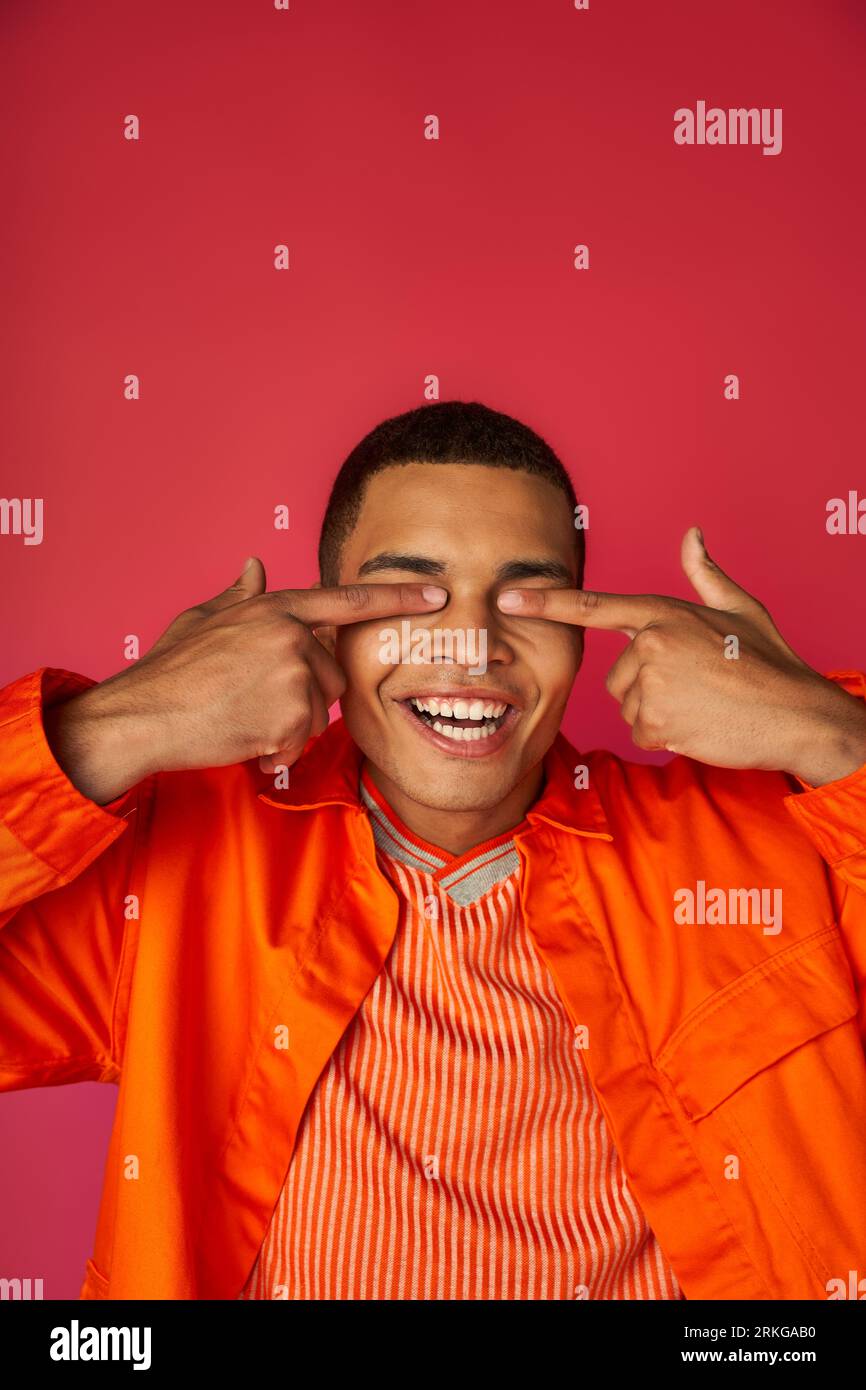 cheerful african american guy obscuring eyes with fingers, orange shirt ...