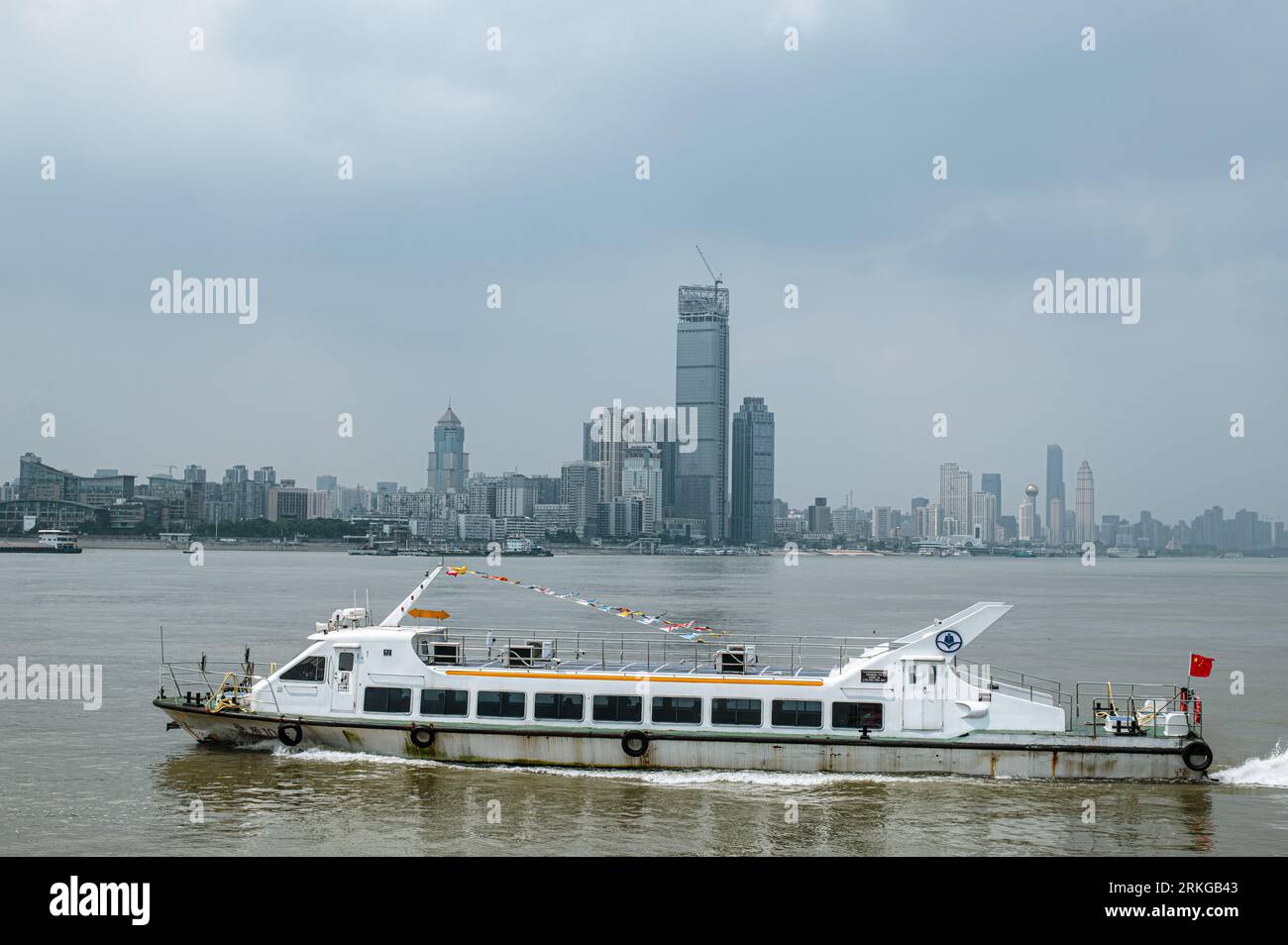 A large, white boat floating in the water in front of the Wuhan skyline ...