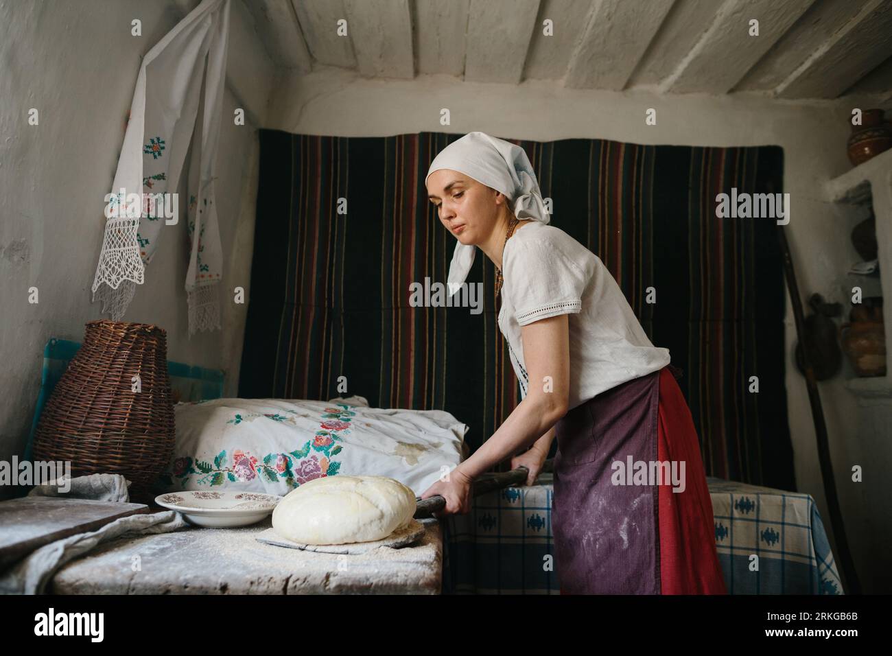 A woman in national Ukrainian dress puts bread in a wood-burning oven ...
